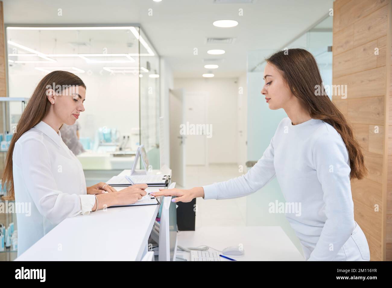 Clinic patient signing document at reception desk assisted by secretary ...
