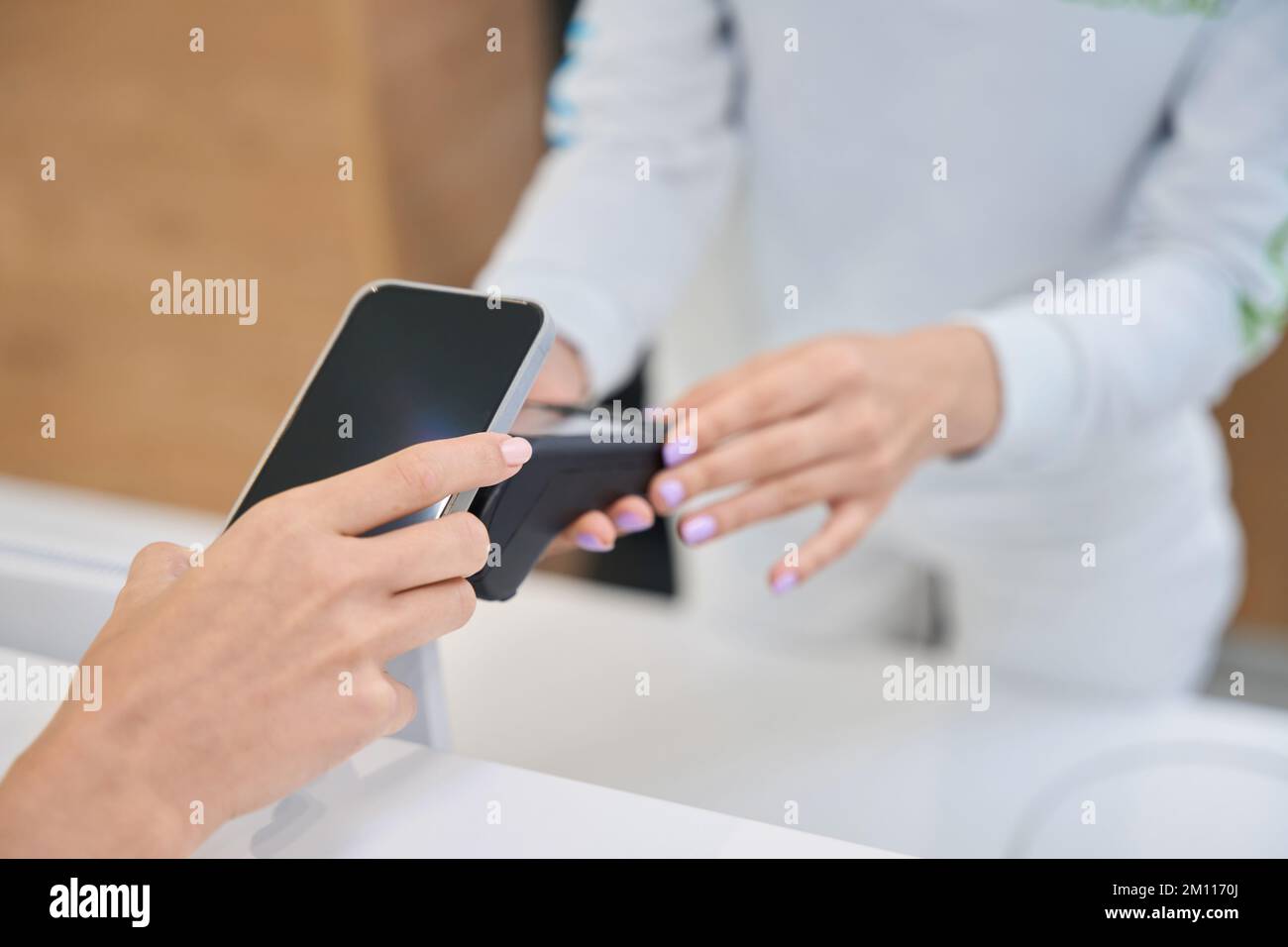 Client paying with mobile phone at reception desk Stock Photo - Alamy