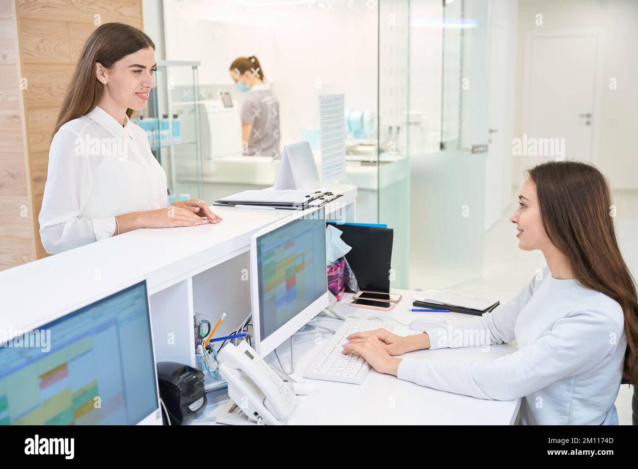 Pleased female patient communicating with friendly secretary in medical ...