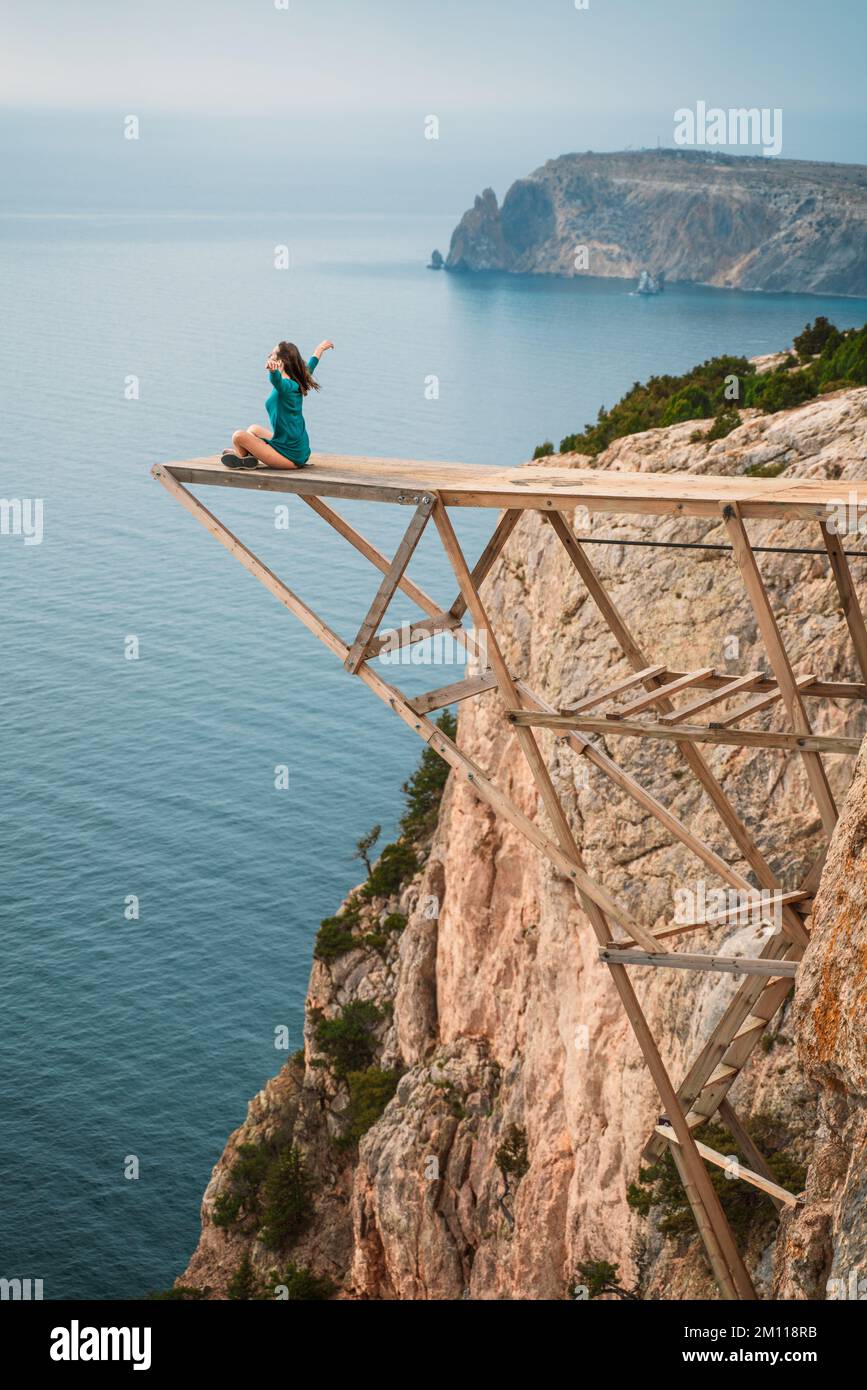A girl sits on a wooden springboard for jumping with a rope. In a dark ...