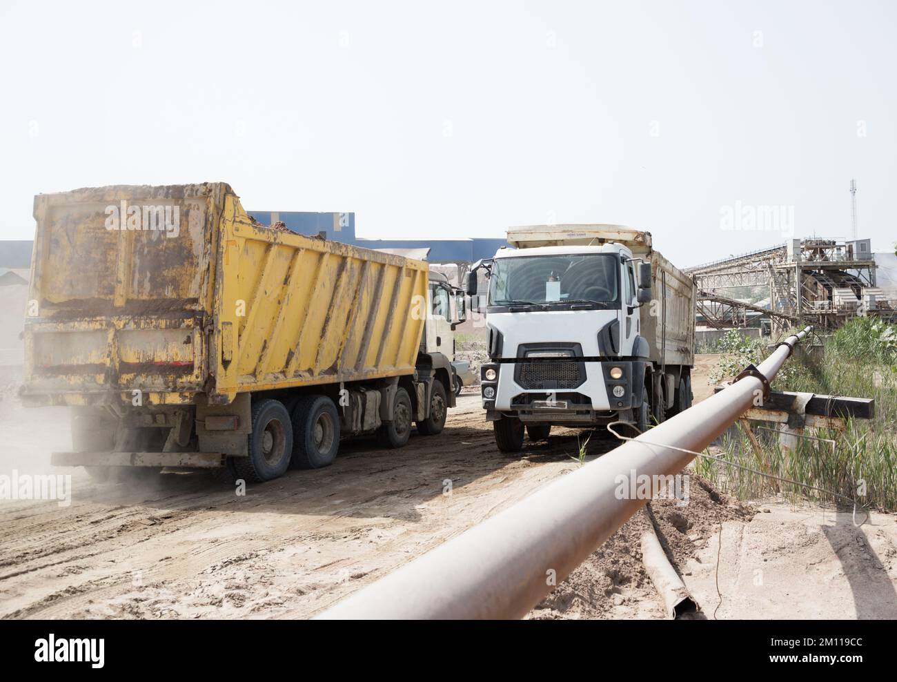two dump trucks are driving in opposite direction on sandy road. Dust ...