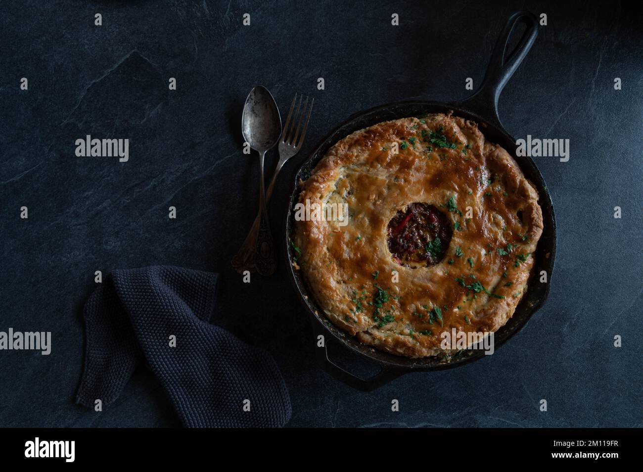 Minced meat pie in a cast iron pan isolated on dark wooden table ...
