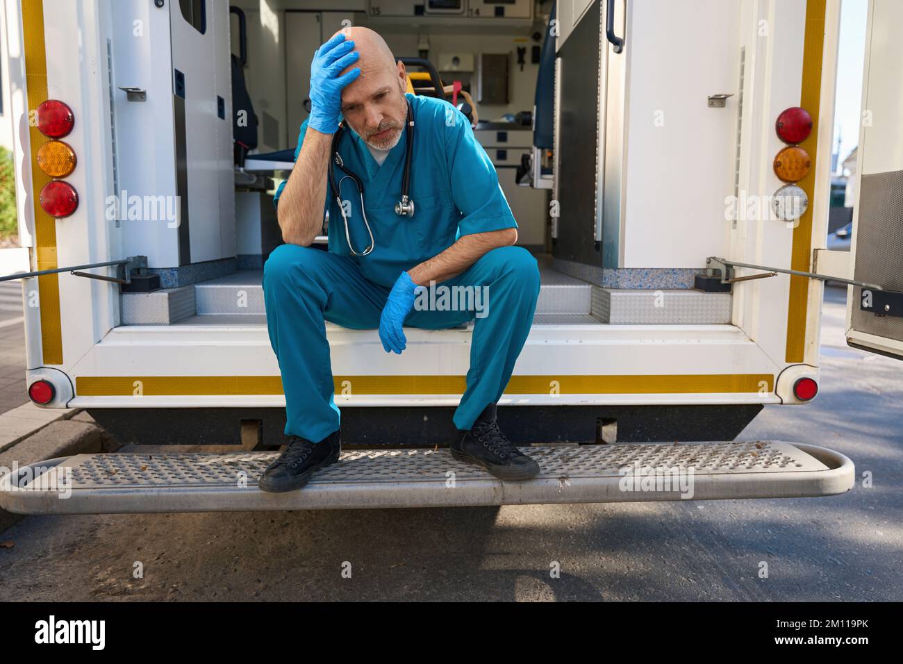 Doctor crouched while working on road and touches head with hand Stock ...