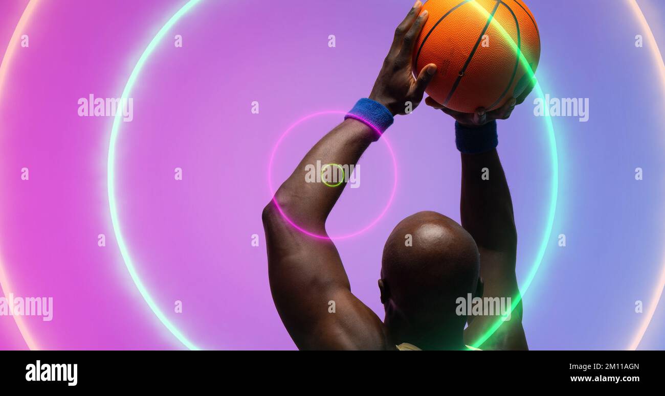 Bald african american basketball player throwing ball over illuminated ...