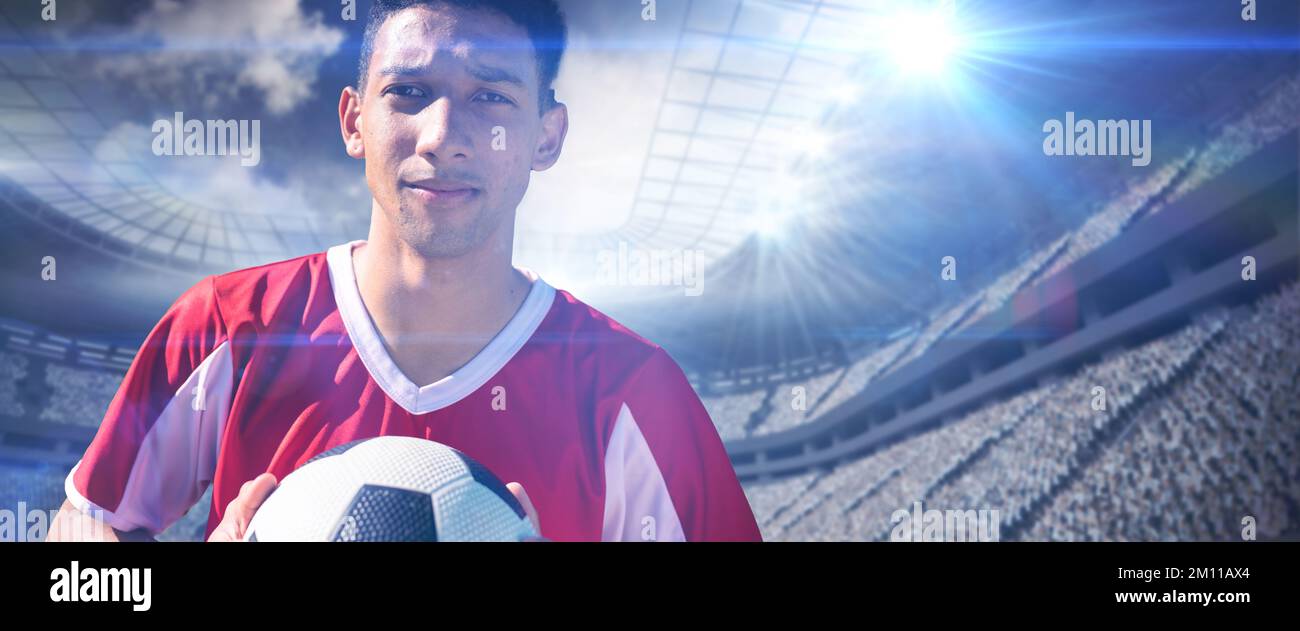Portrait of confident biracial young soccer player with ball in stadium ...