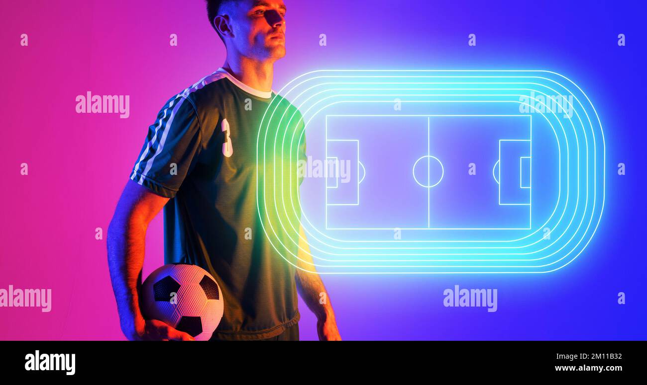 Caucasian young player holding ball by neon soccer field in blue and ...