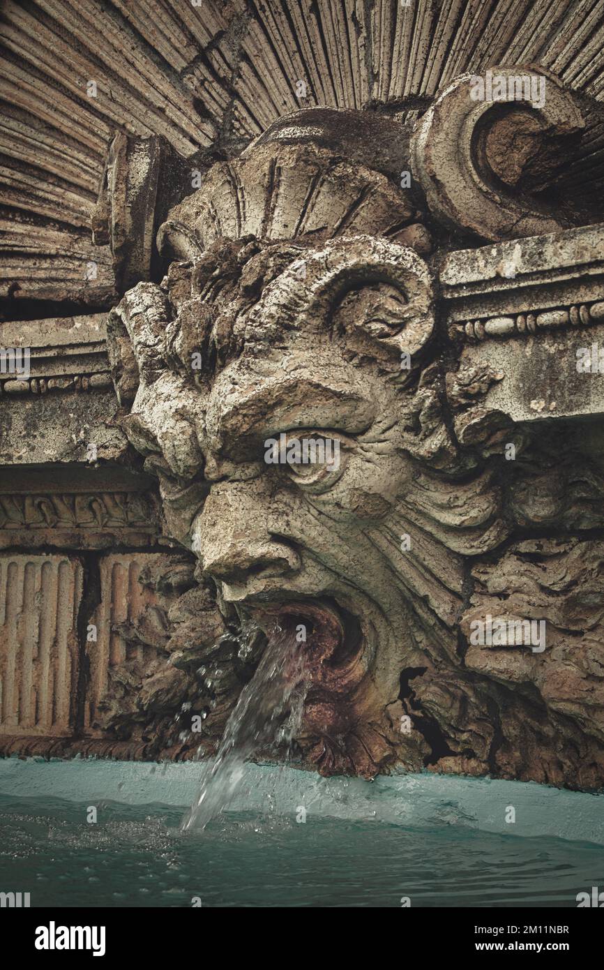 An abstract sculpture of a beast's face on the wall with water coming ...