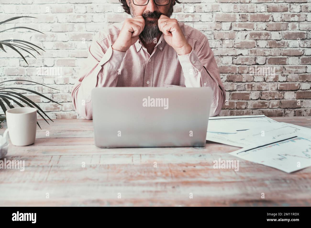 Front view of man working at the desk with laptop and paper charts ...