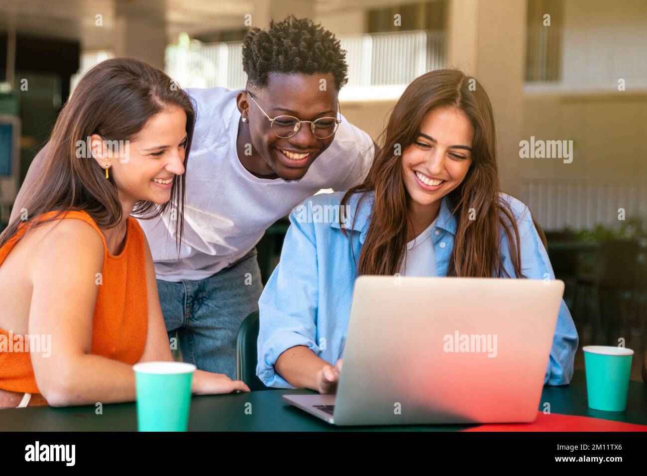 Group of happy friends students sitting in a cafe bar looking at laptop ...