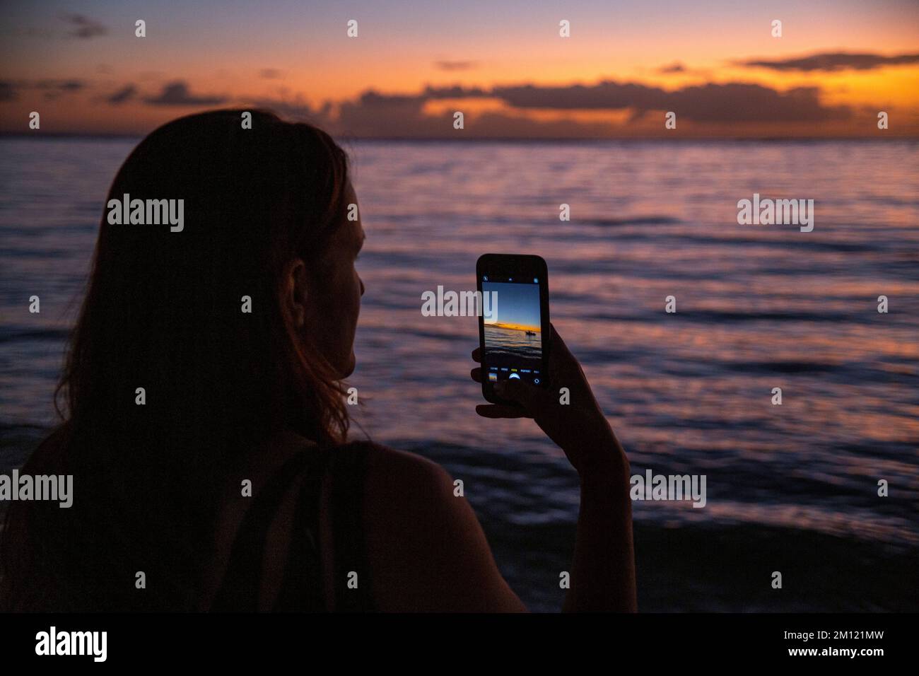 A young lady taking a picture of the sunset at a beach in Mauritius ...