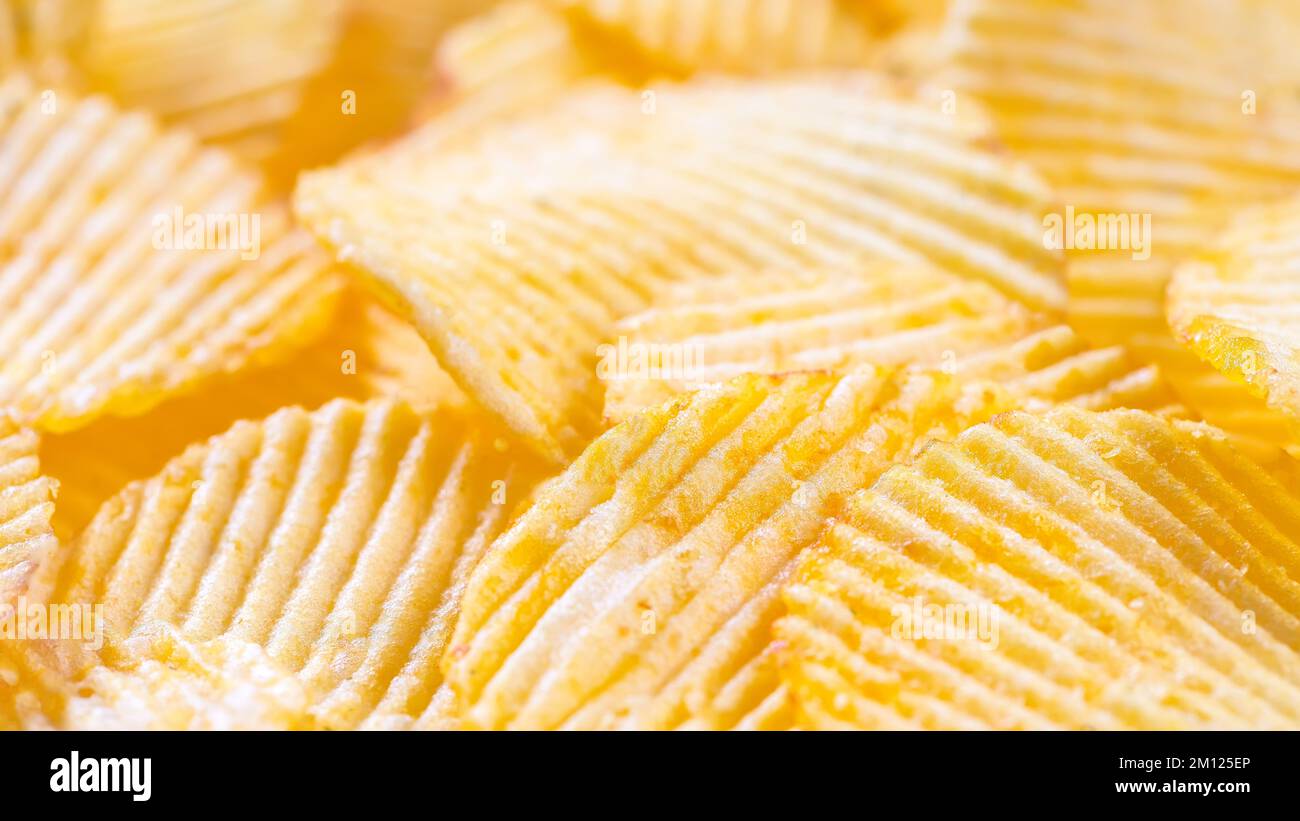 Yellow crispy ridged potato chips close up. Food background, banner ...