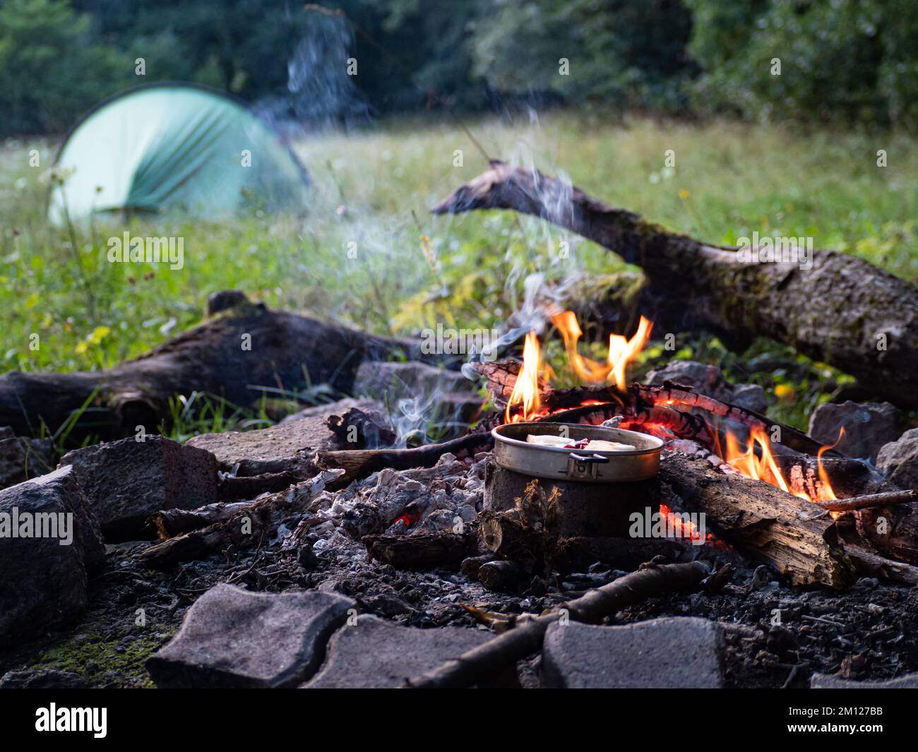 Outdoor camping cooking on a campfire with tent in the blurry ...