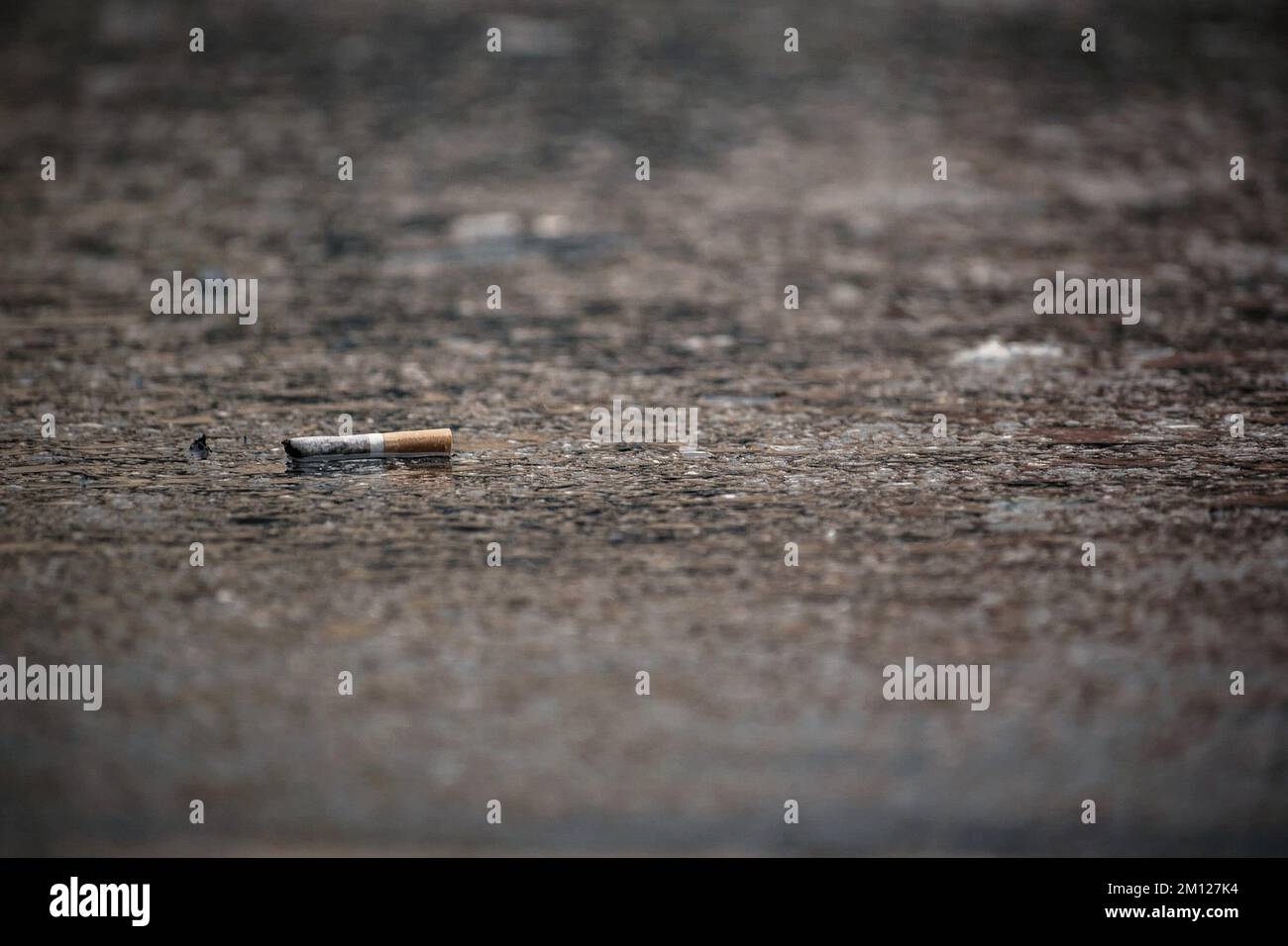 A selective focus shot of a half smoked cigarette on a wet pavement ...