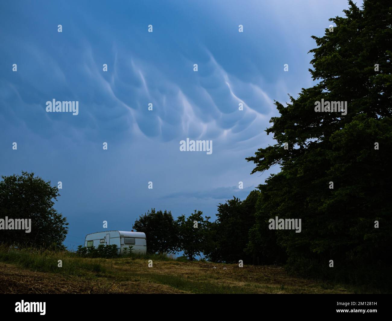 Before a storm mammatus clouds are gathering over a camper trees field ...