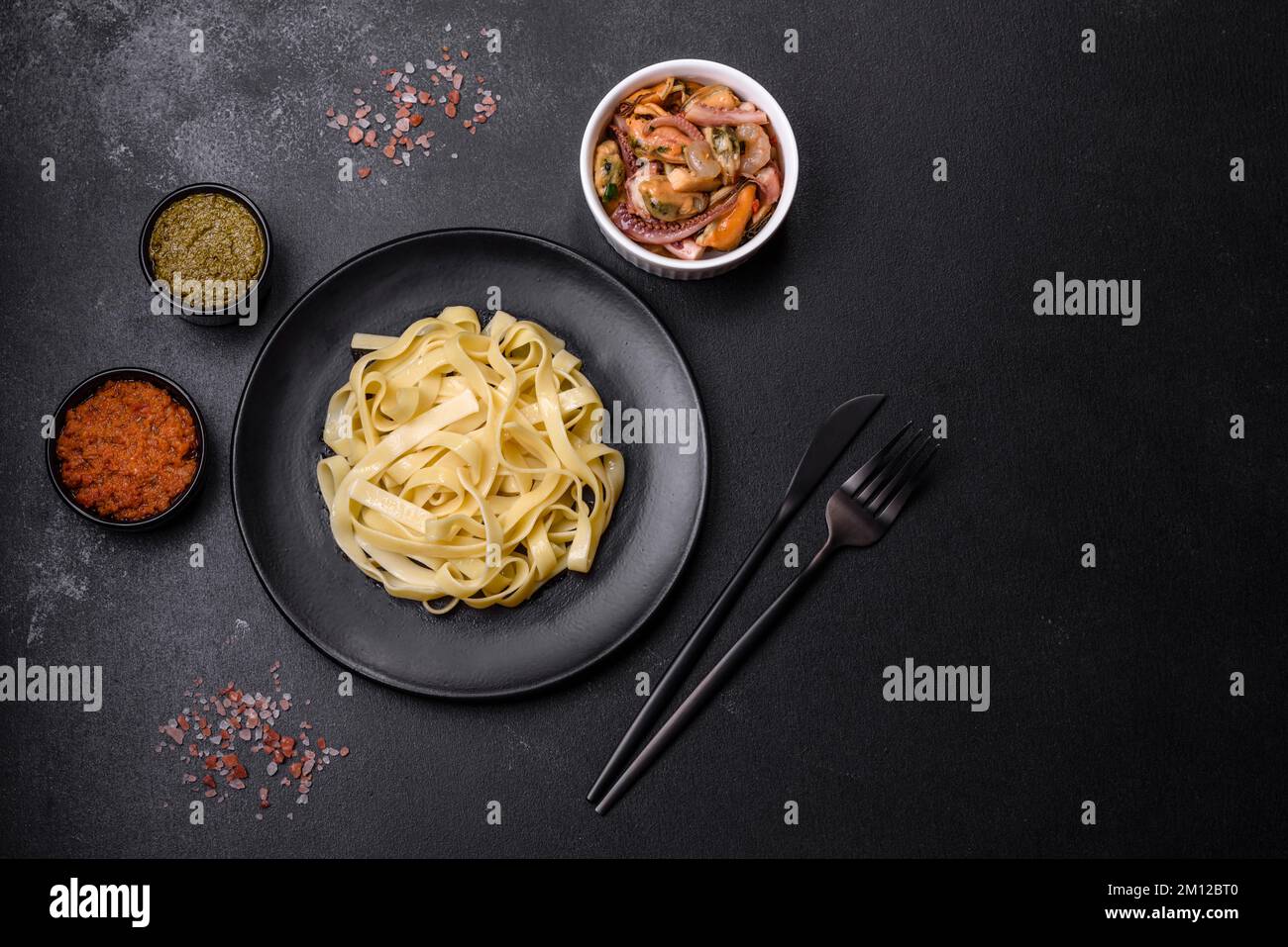 Delicious fresh pasta with pesto sauce and seafood on a black plate ...