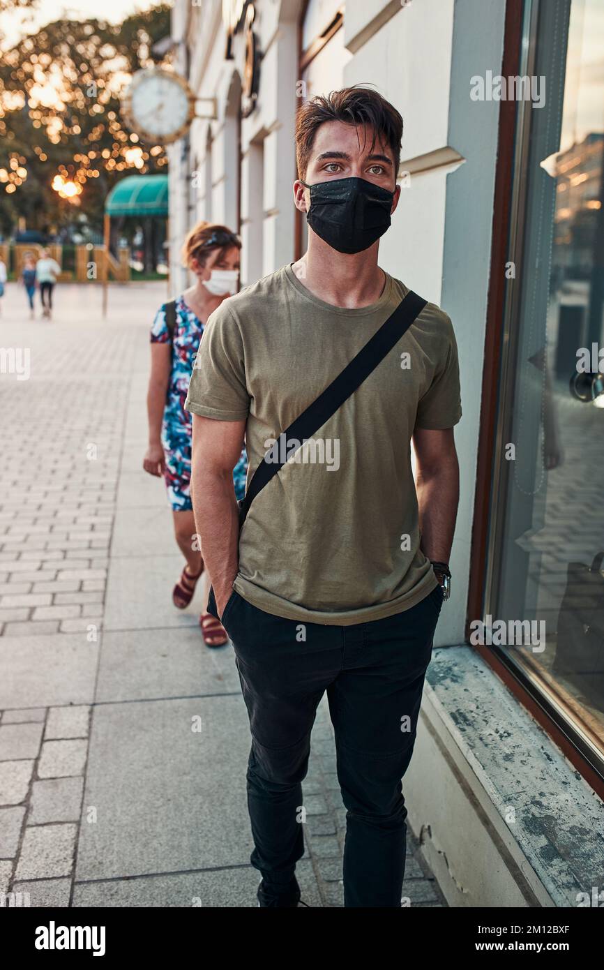 Young man walking along a store front in the city center in the evening ...