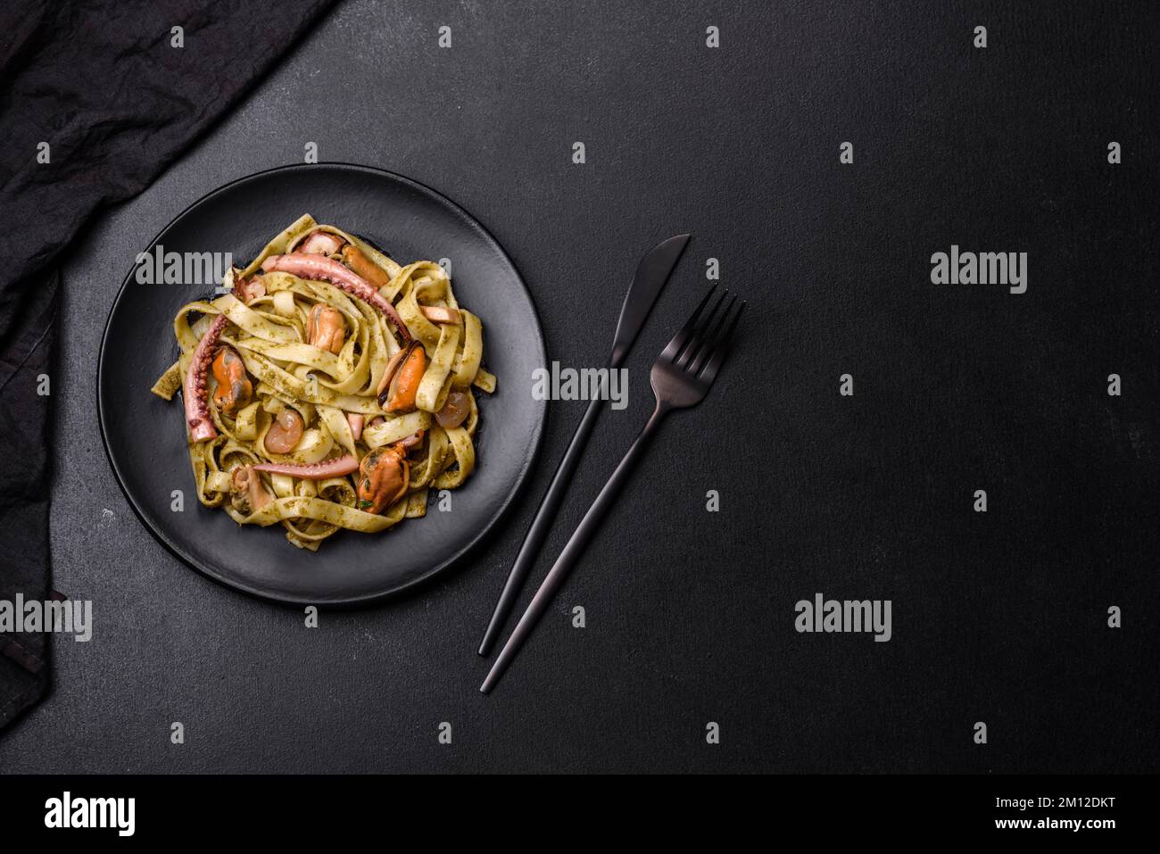 Delicious fresh pasta with pesto sauce and seafood on a black plate ...