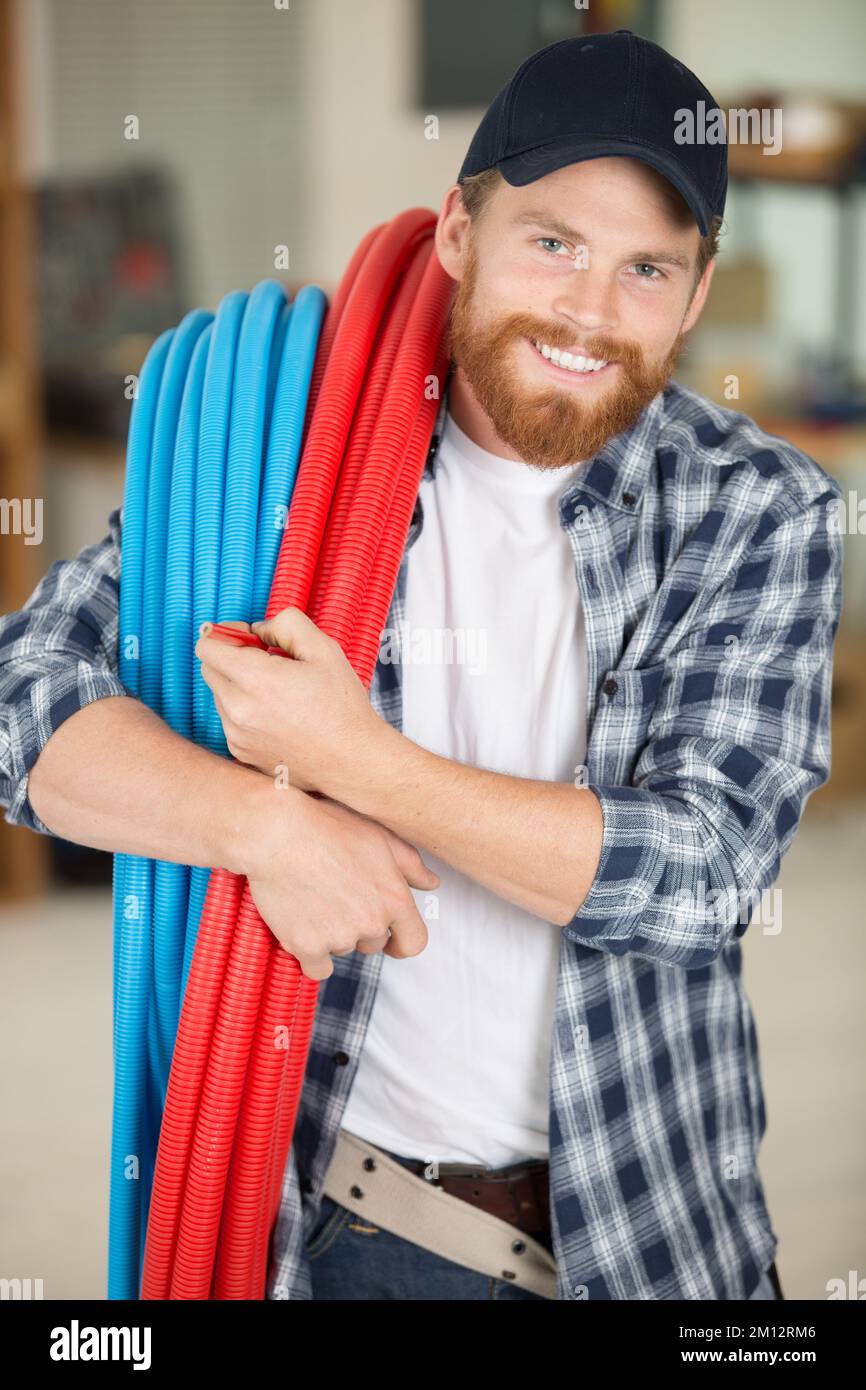 a builder with reel of blue pipe over his shoulder Stock Photo - Alamy