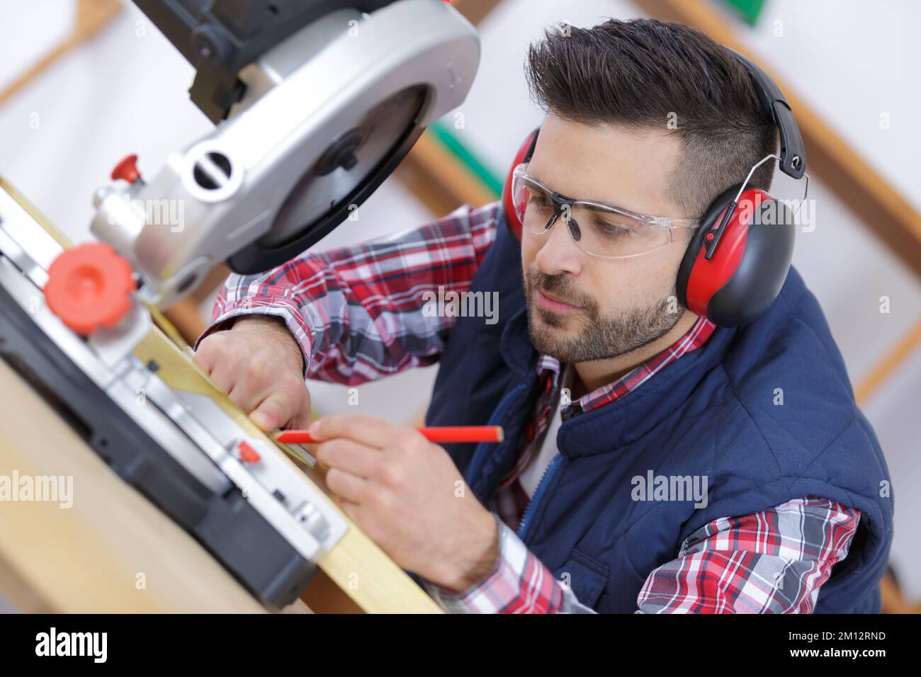 craftsman wearing protective equipment measuring wood by circular saw ...