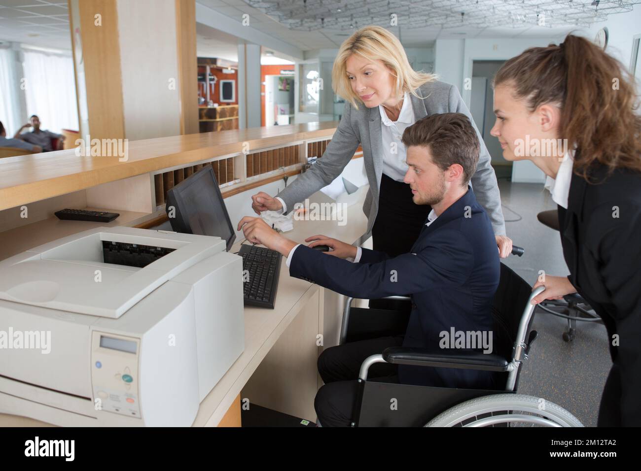 Staff behind reception desk, young man in wheelchair Stock Photo - Alamy
