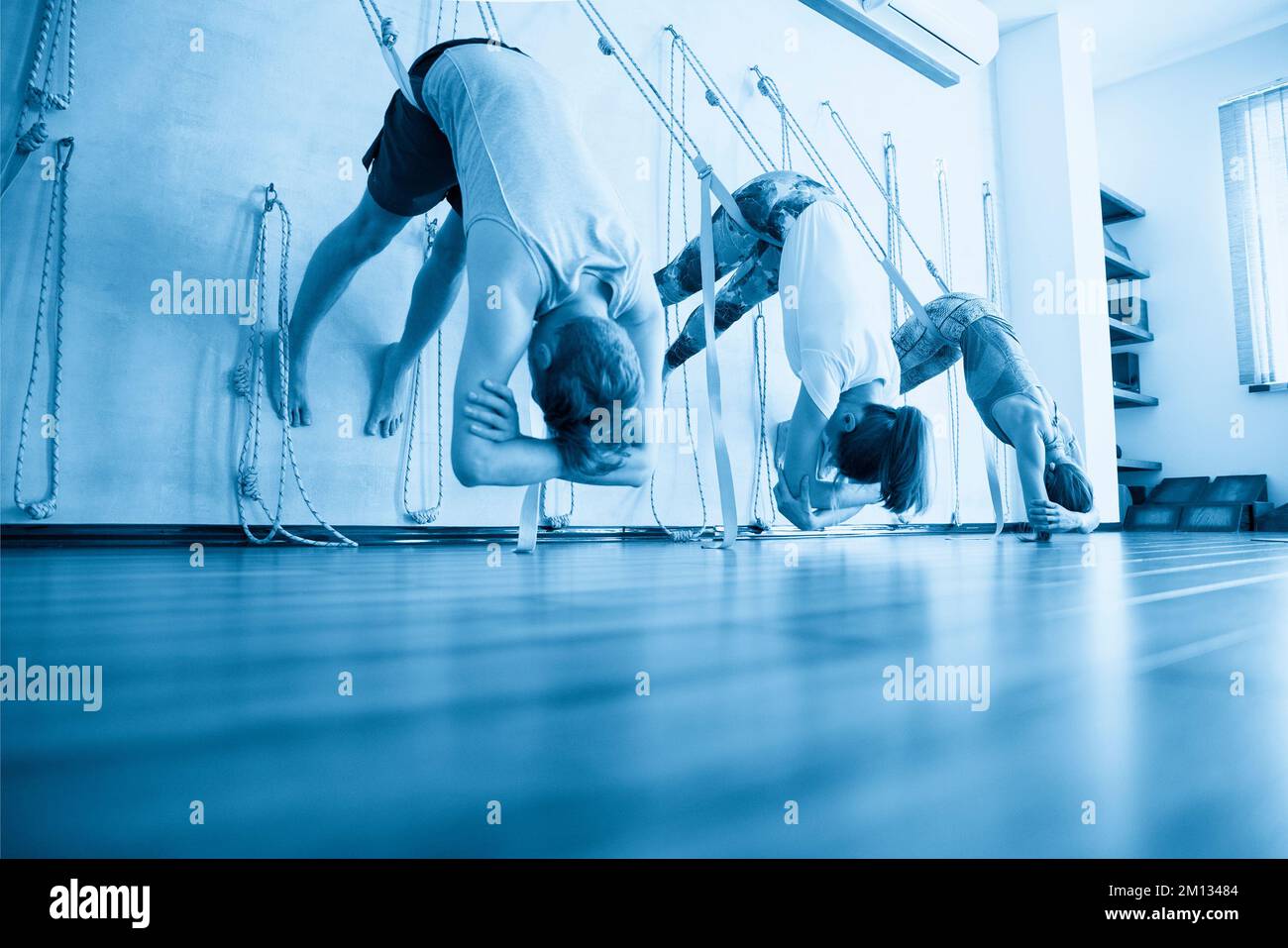 People hanging on ropes practicing yoga stretching in gym. Fit and ...