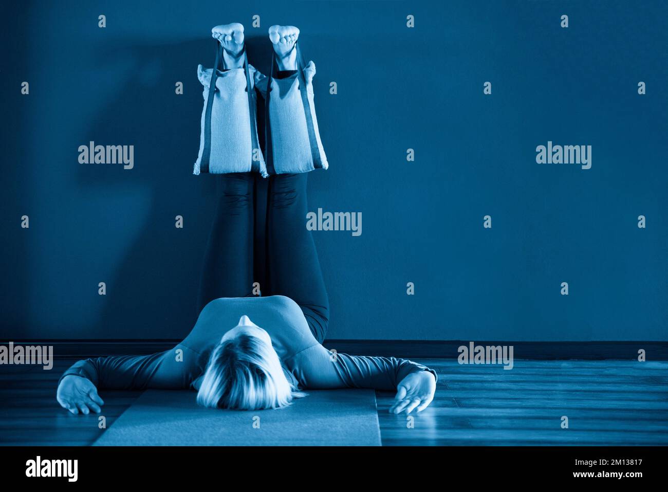 Young woman in yoga relaxing pose with legs up against wall with heavy ...