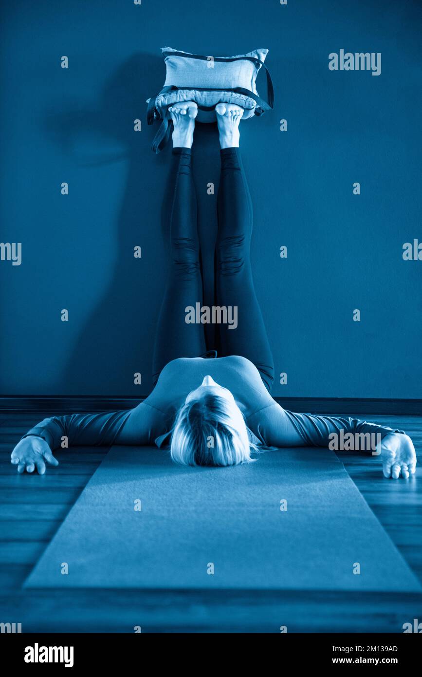 Young woman in yoga relaxing pose with legs up against wall with heavy ...