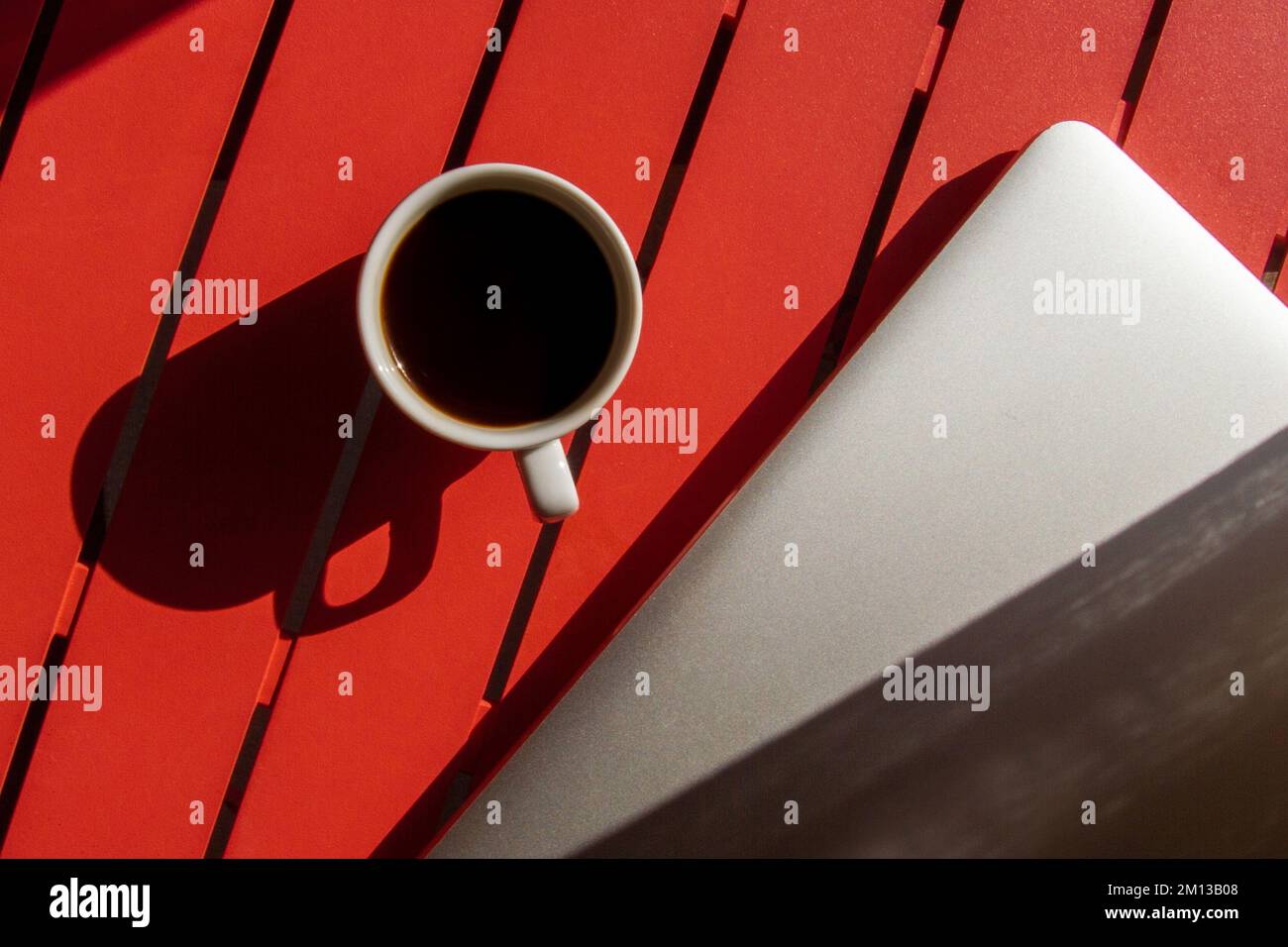 A cup of coffee and a laptop on a red table. Kind of light. Hard light ...