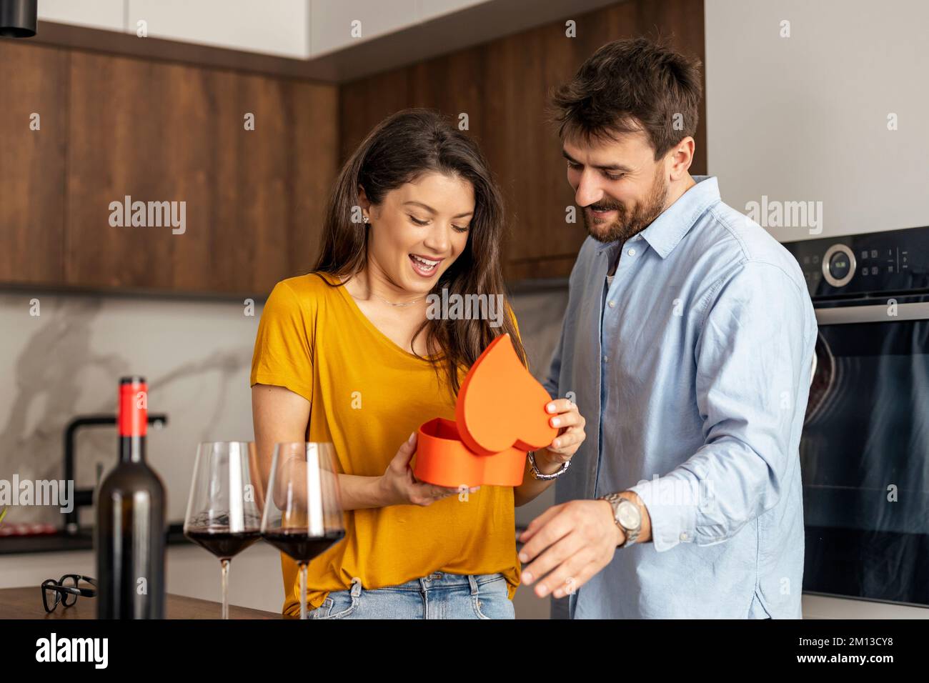 Husband and wife relaxing together in kitchen and drinking wine ...