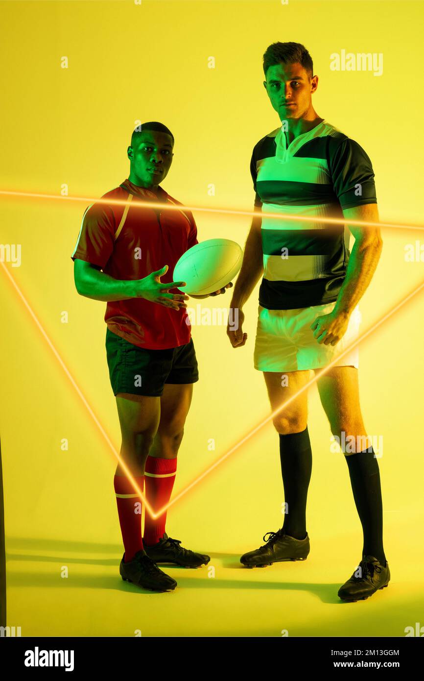 Multiracial male rugby opponents with ball standing by illuminated ...