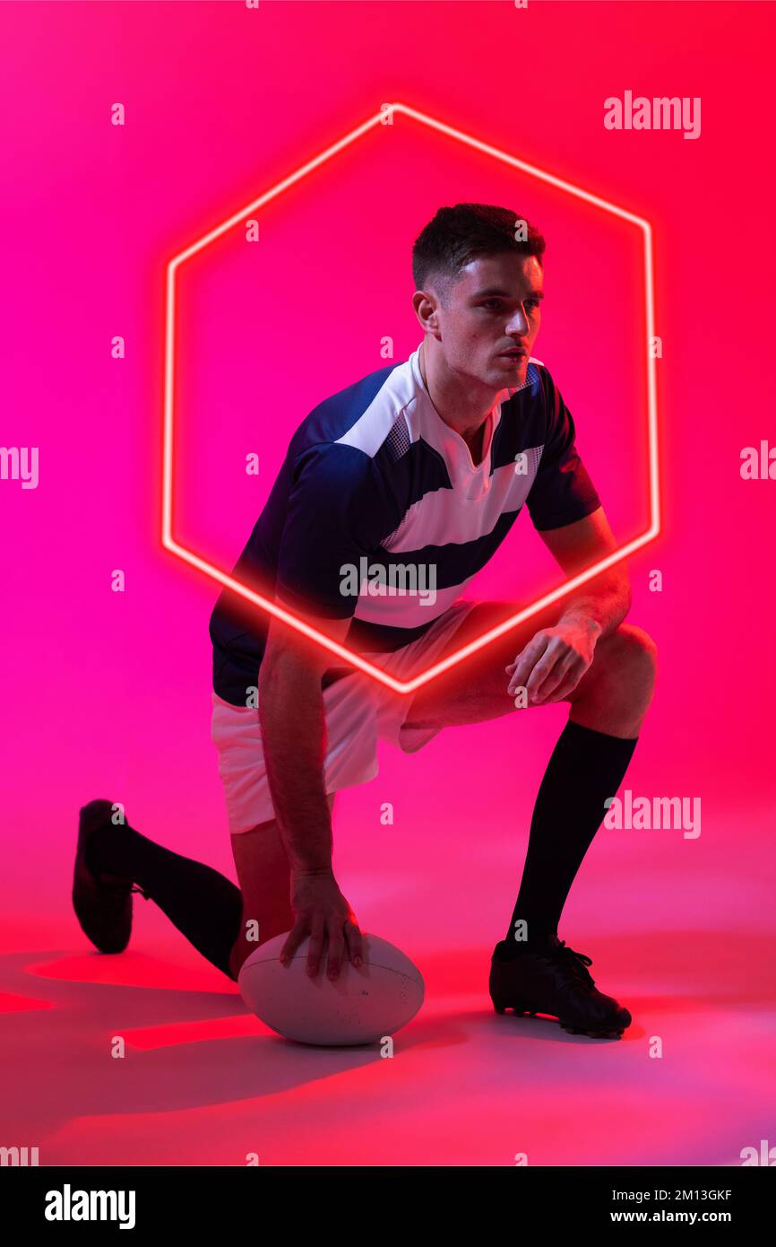 Caucasian male rugby player with ball kneeling by illuminated hexagon ...