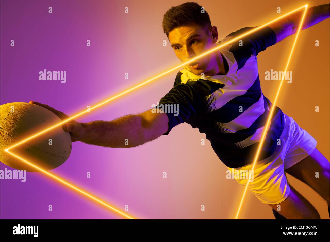 Caucasian male rugby player holding ball and jumping by illuminated ...