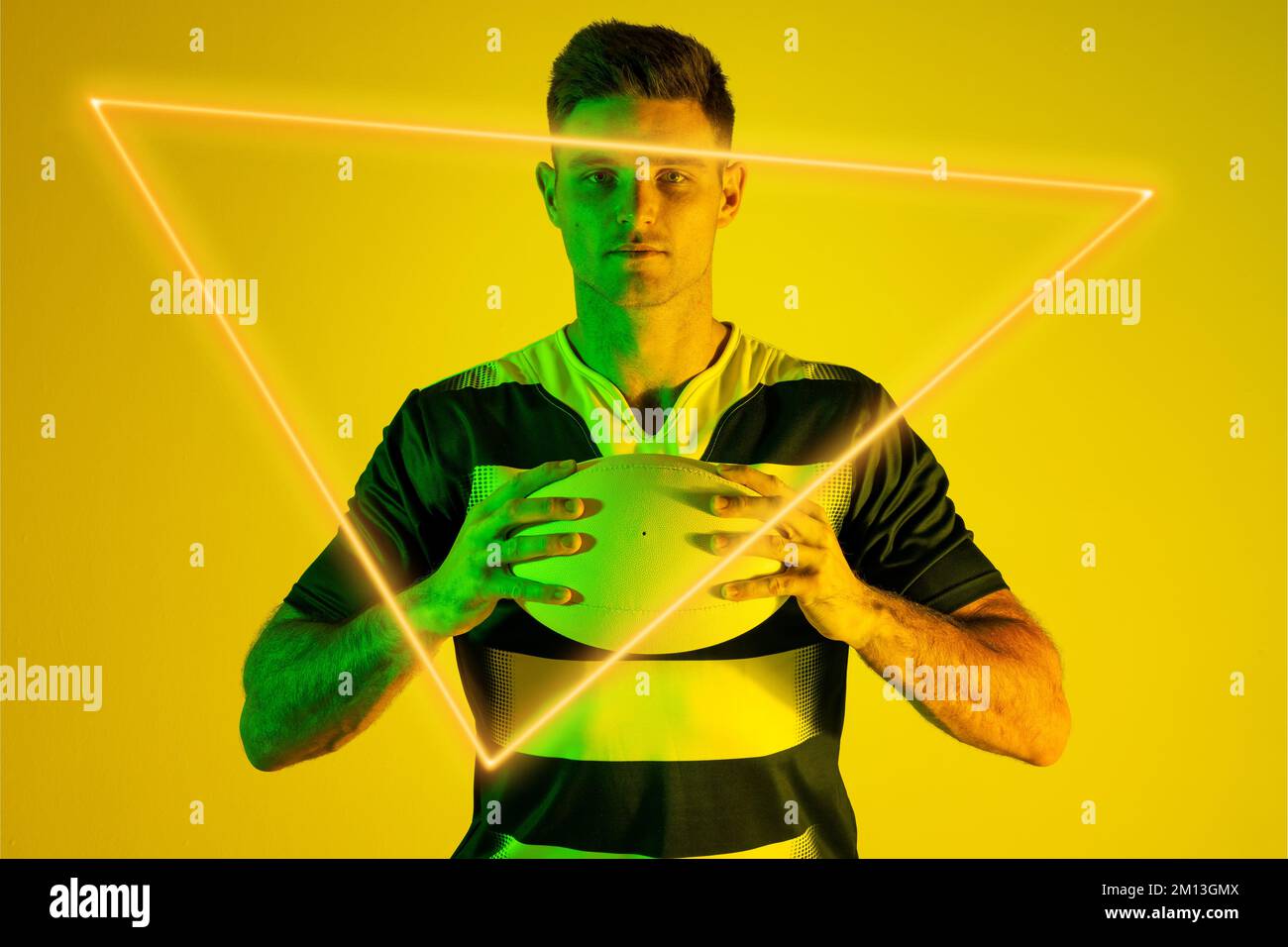 Portrait of caucasian male rugby player holding ball by illuminated ...