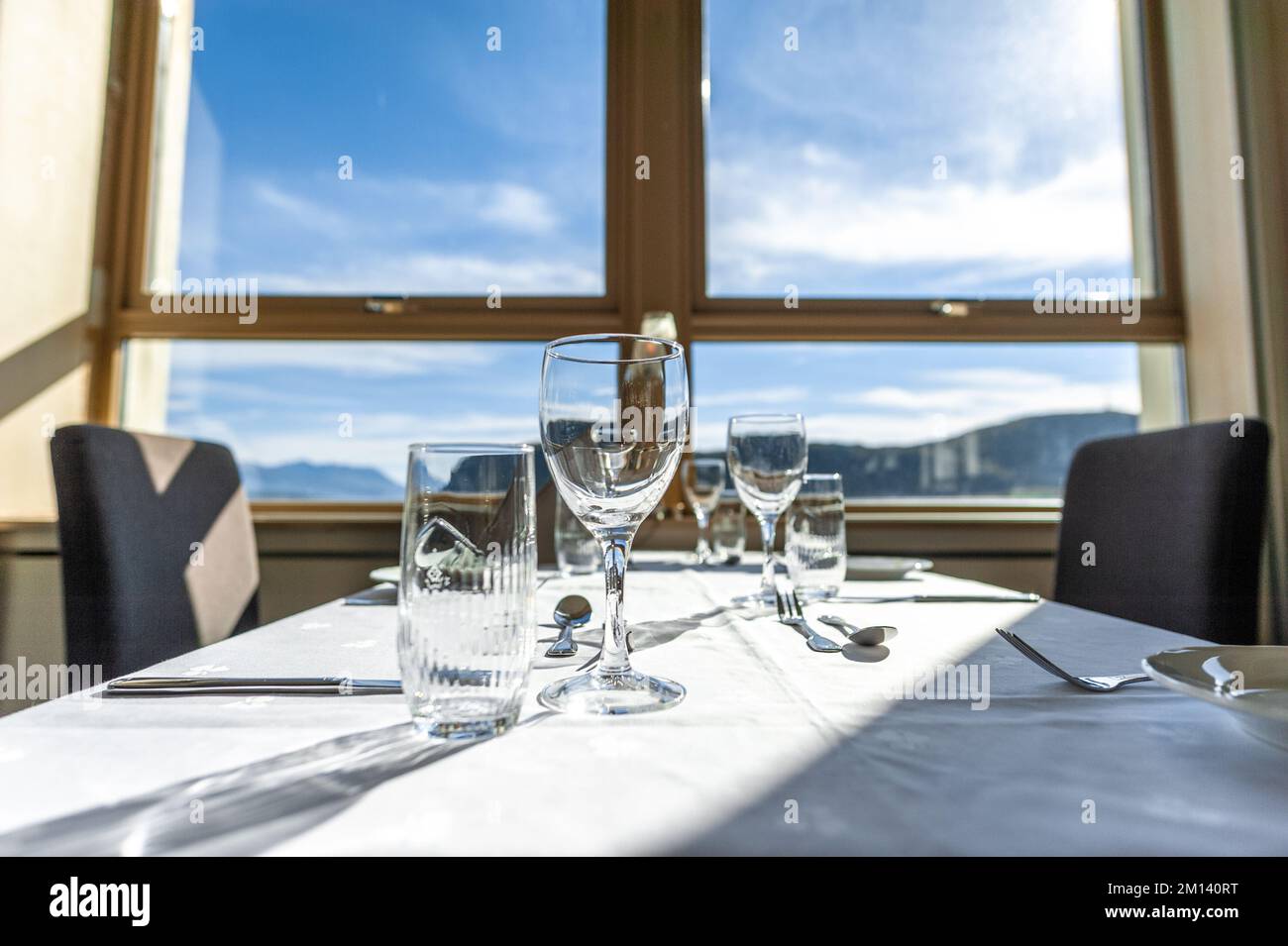 An empty dining table with glass cups, spoons, forks and knives near a ...