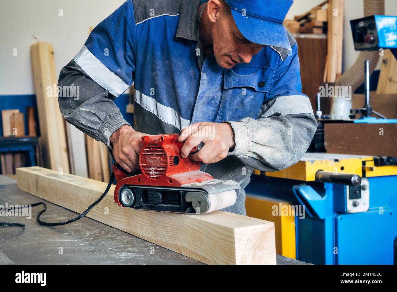 Carpenter in work clothes processes wood with grinder. Polishing of ...