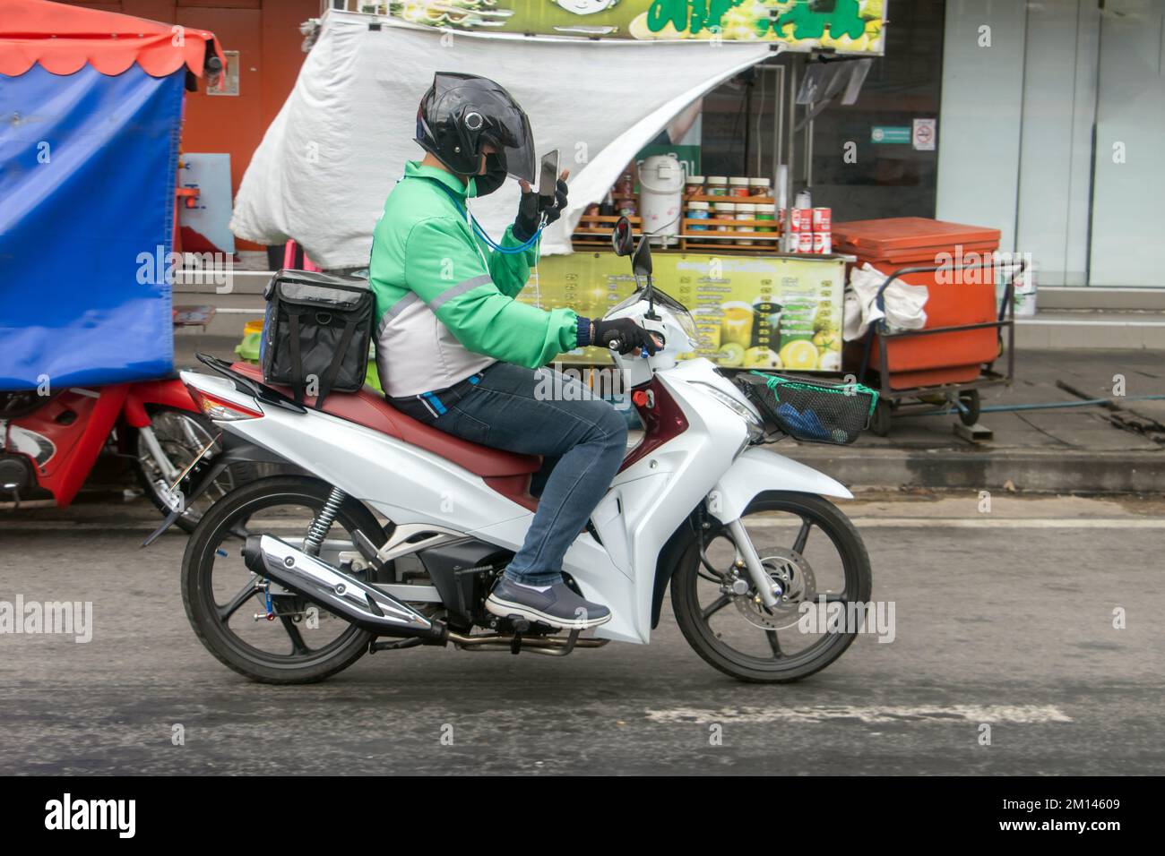 A delivery worker rides a motorcycle with a shipments and looks to his ...