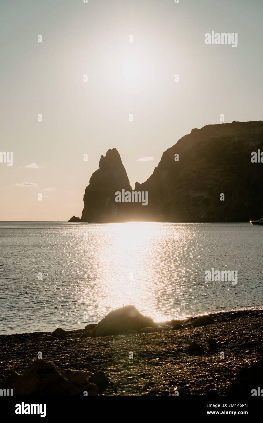 A red burning sunset over the sea with rocky volcanic cliff. Abstract ...