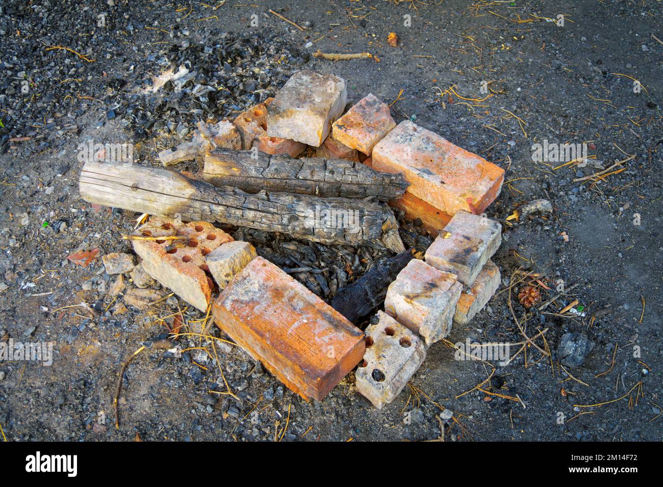 An extinguished red brick hearth with charred firewood in the forest ...
