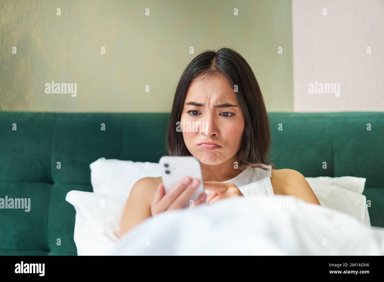 Close up portrait of grumpy asian girl lying in bed, grimacing and ...