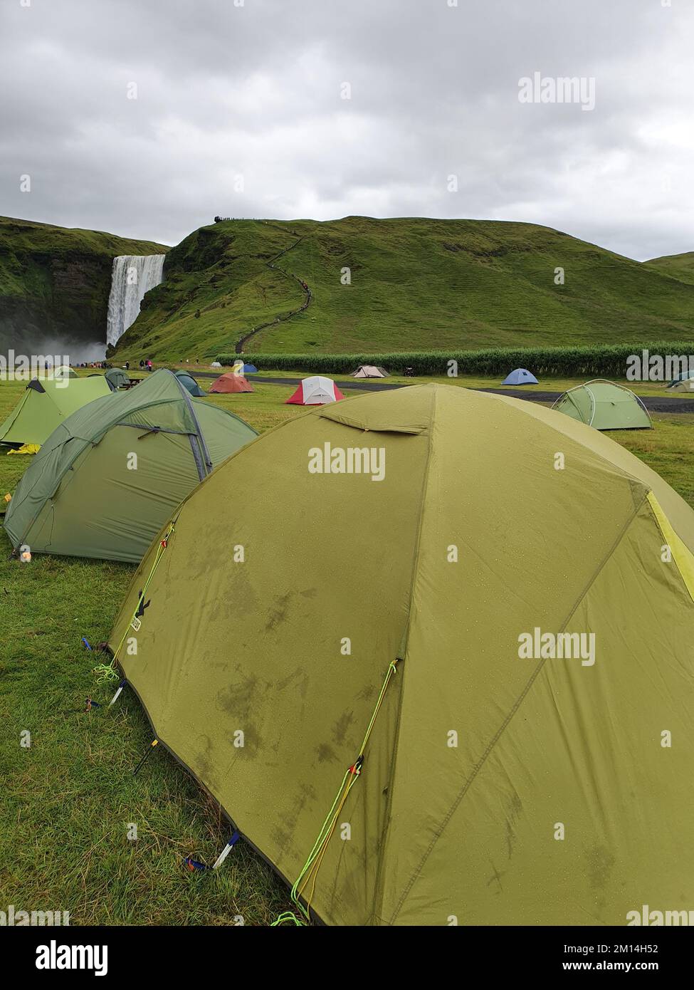 A vertical shot of green tents placed in front of the Seljalandsfoss ...