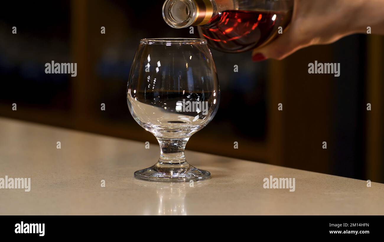 Close up of woman hand pouring cognac to the glass standing on the bar ...