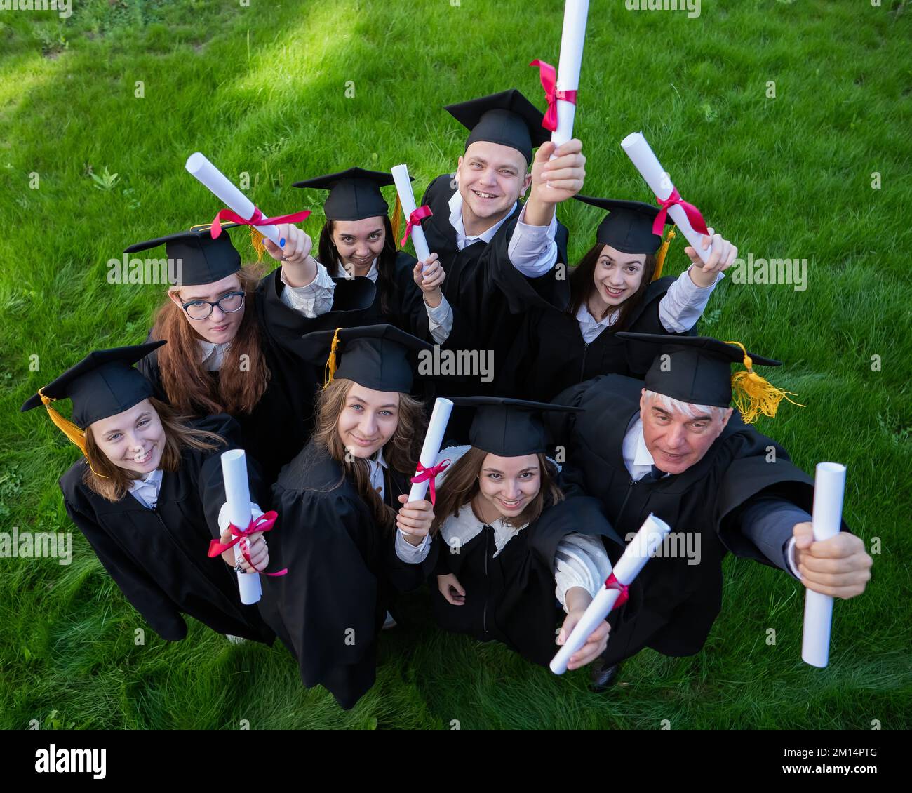 Graduates in robes show off their diplomas outdoors. View from above ...