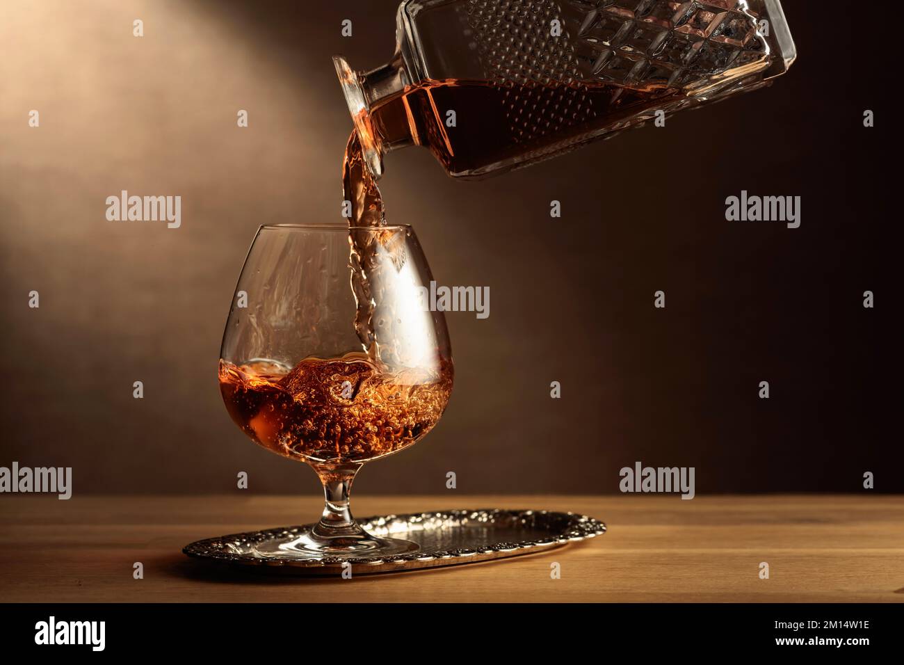 Brandy is poured from a decanter into a snifter glass. Cognac on an oak ...