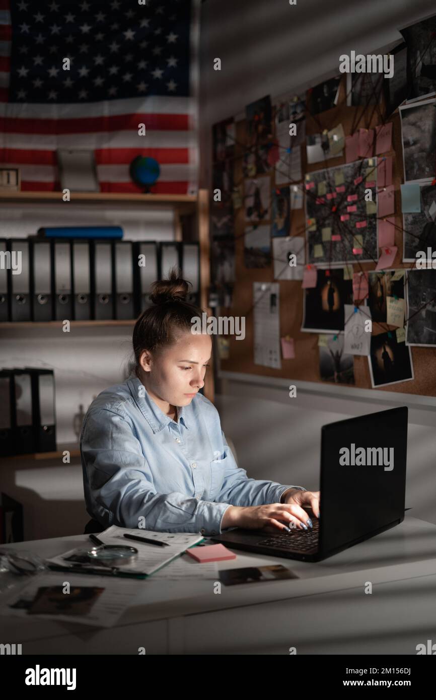 Detective processing evidence in office using laptop computer at night ...