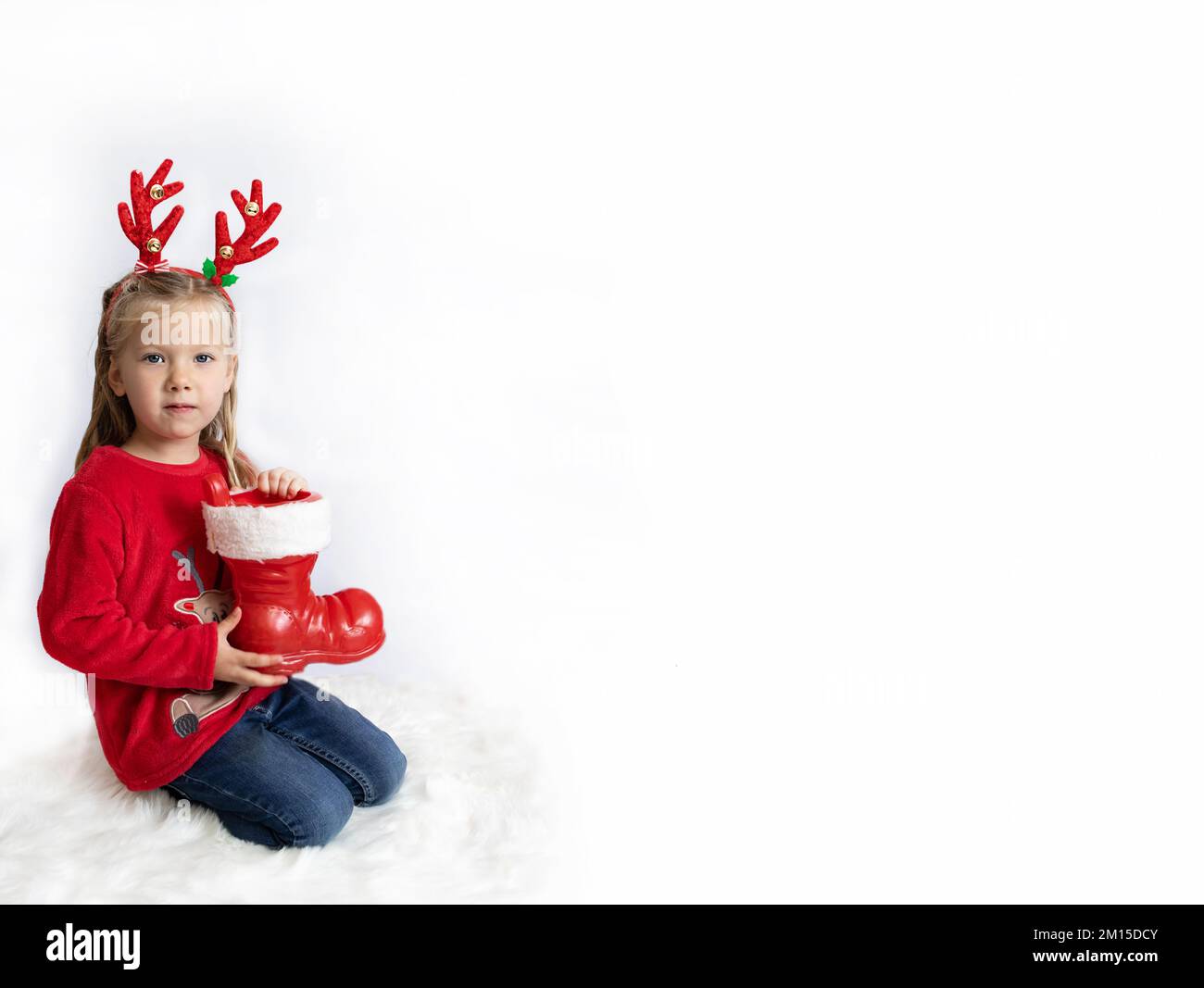 Christmas. A girl with deer horns in a red sweater holds santa boots ...