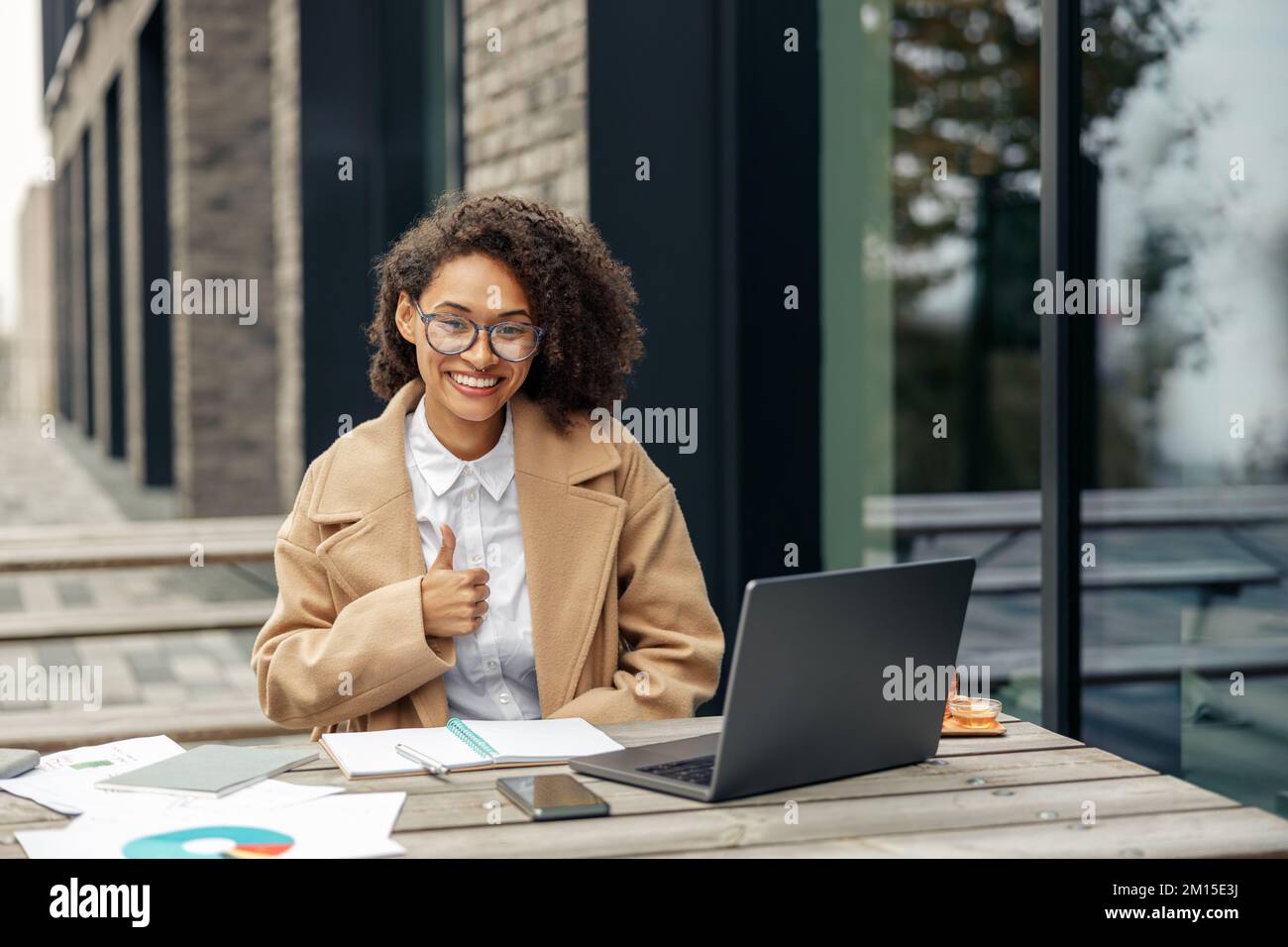 Smiling african business woman showing thumb up while working laptop ...