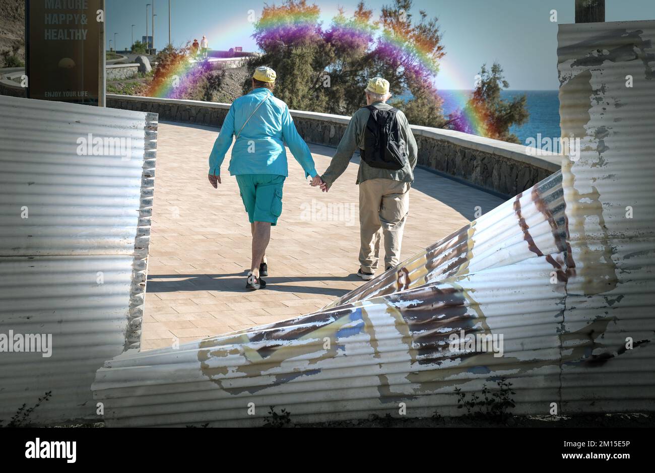 Retired couple walking hand in hand on the promenade, towards a rainbow ...