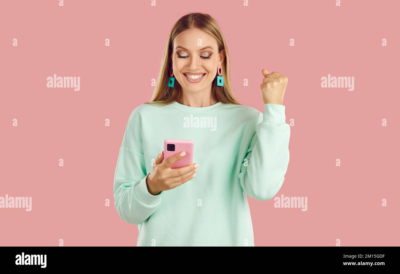 Happy lucky blondy girl is showing yes gesture looking at smartphone on ...