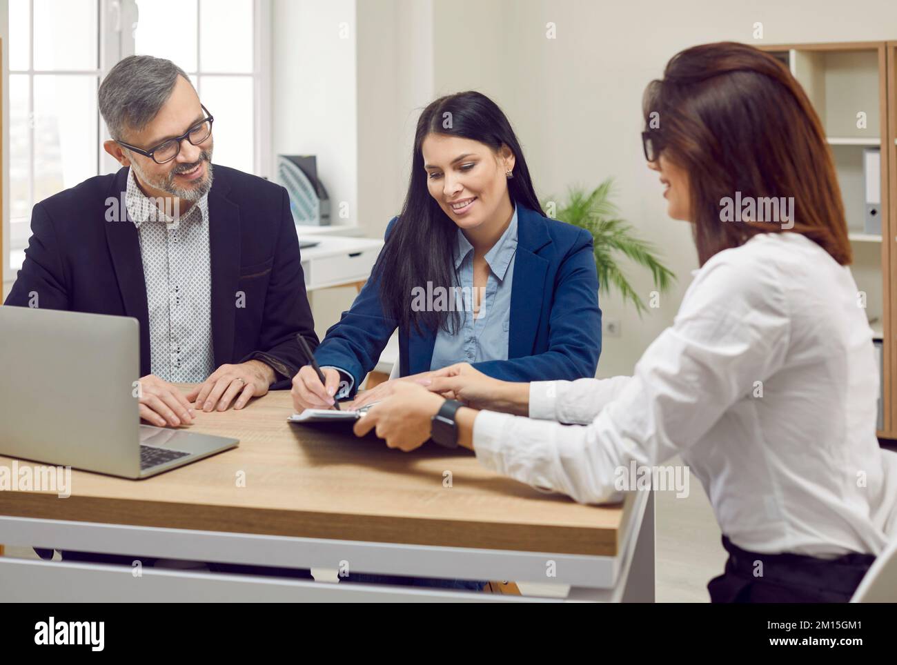 Happy couple who are clients of bank signs paper document confirming ...