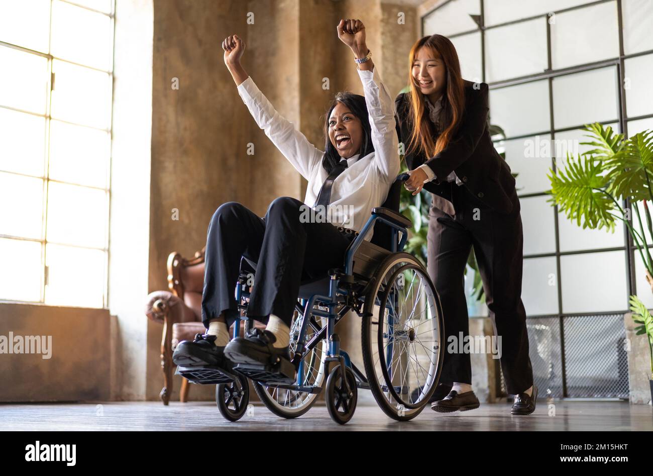 Young asian woman pushing african american collegue in wheelchair in co ...